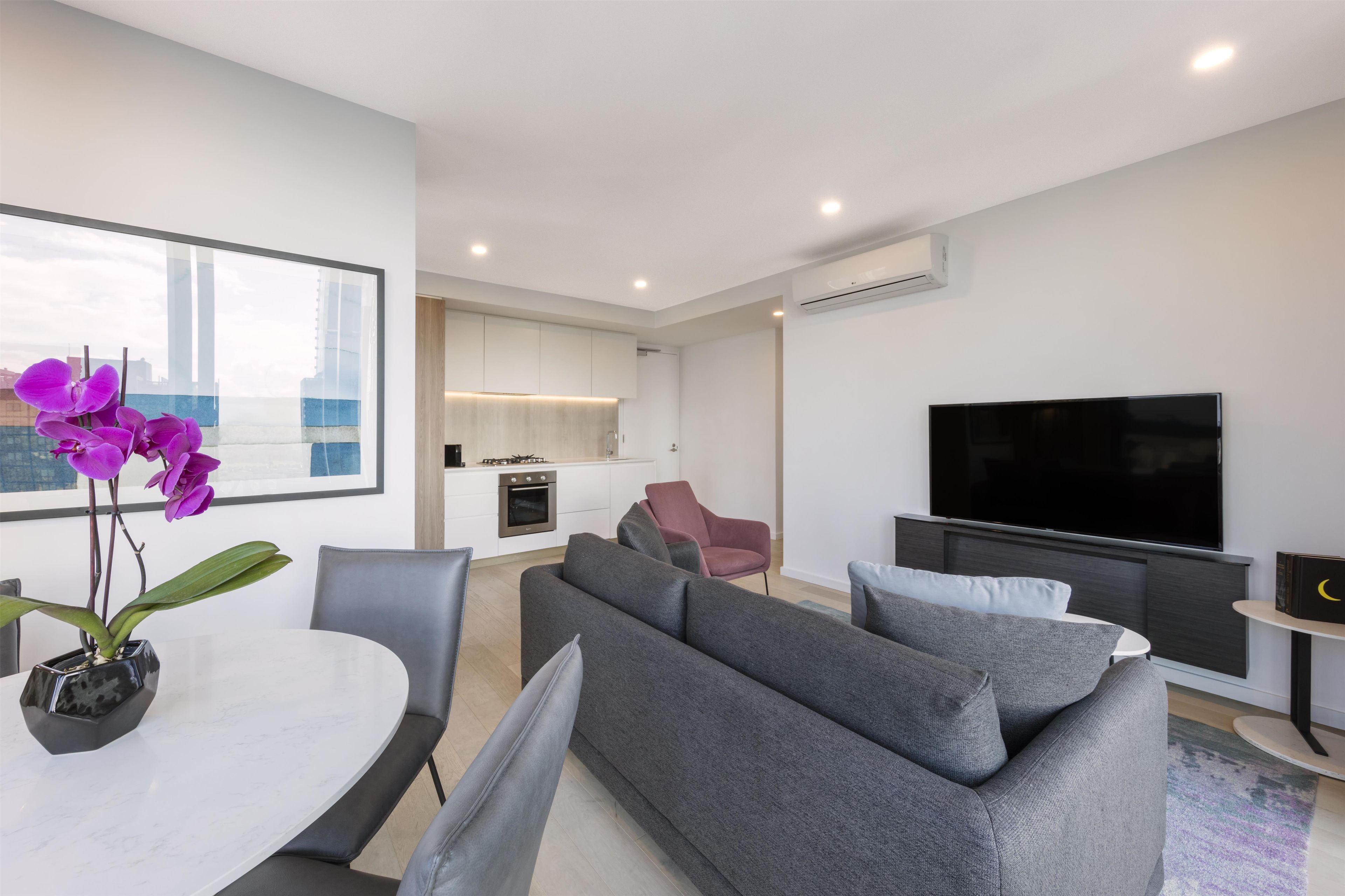 Uma sala de estar moderna com um sofá cinzento, uma televisão de ecrã plano e um espaço de refeições com mesa e cadeiras.