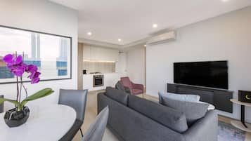 Uma sala de estar moderna com um sofá cinzento, uma televisão de ecrã plano e um espaço de refeições com mesa e cadeiras.