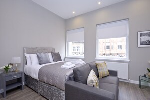 Um quarto moderno com cama, mesa de cabeceira e um sofá.