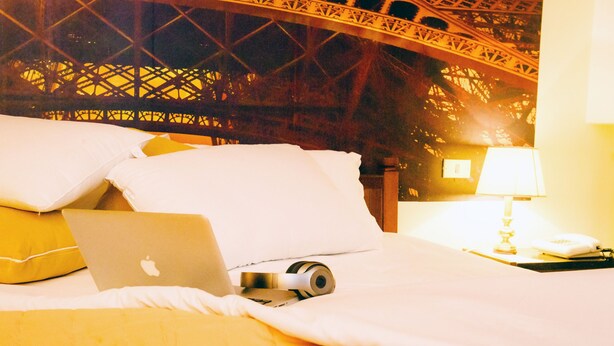 Cama com um laptop, uma câmera e uma luminária em uma mesa de cabeceira.