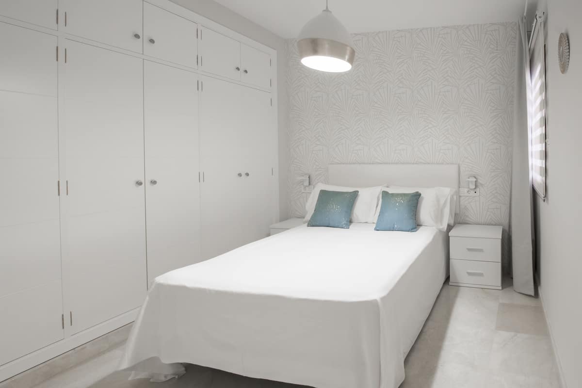 Quarto com cama, guarda-roupa branco, mesas de cabeceira e parede estampada.