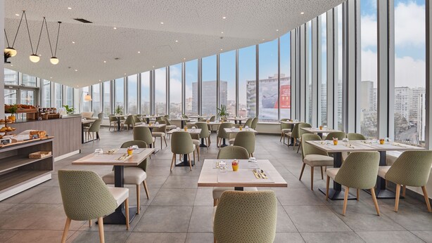Um restaurante moderno com teto alto, janelas grandes e vista para a cidade.