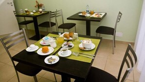 Uma sala de jantar com mesas preparadas para o café da manhã, incluindo pratos de comida, xícaras e talheres.