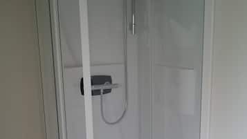 Um chuveiro com paredes de vidro, um chuveiro manual e uma torneira fixada na parede.