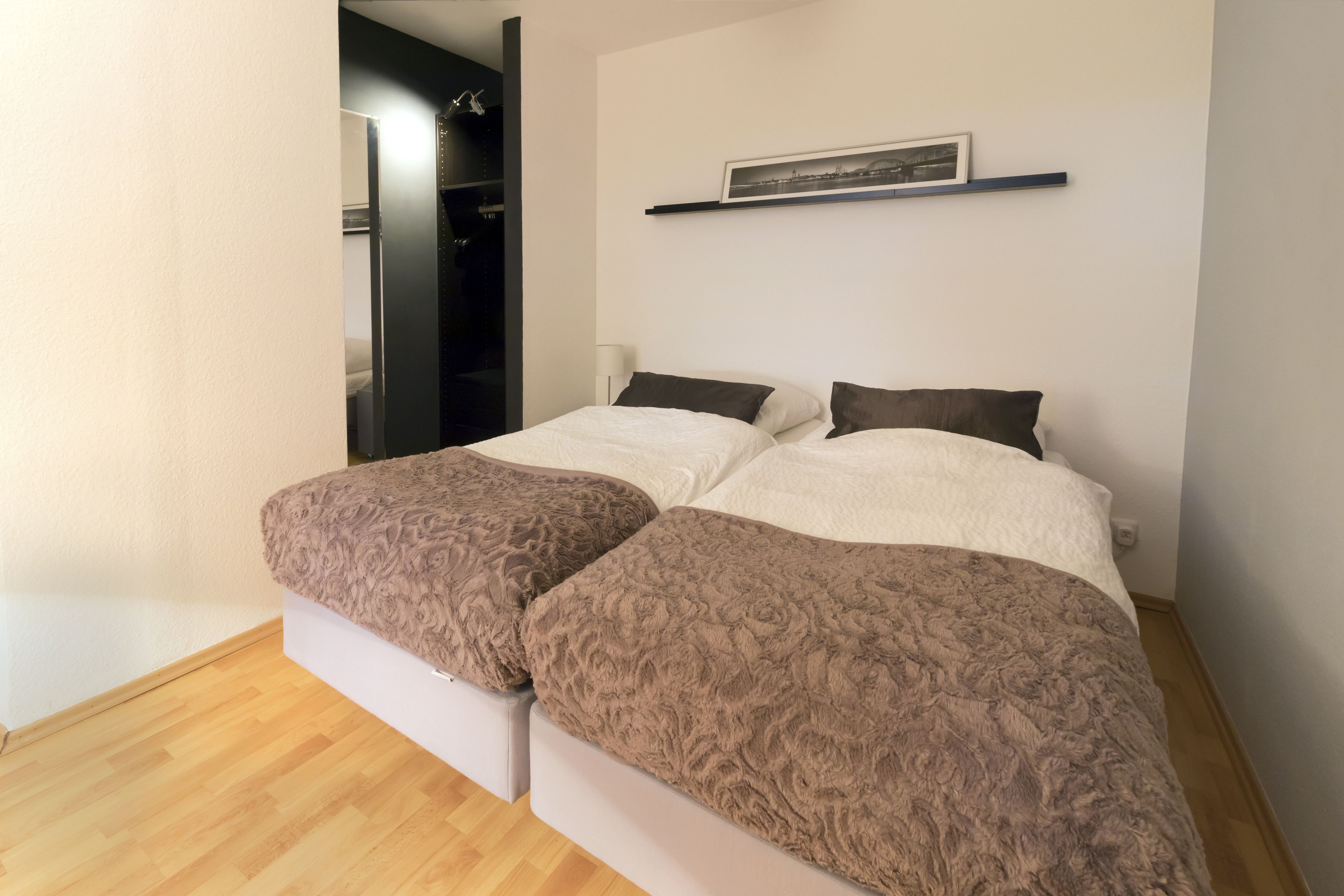 Um quarto com cama, mesa de cabeceira, prateleira na parede com um quadro e porta para um armário.