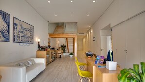Interior moderno com sofá branco, cadeiras amarelas, balcão de recepção em madeira e escada para um andar superior.