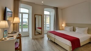 Quarto de hotel com cama, escrivaninha, cadeira e uma janela grande com vista.