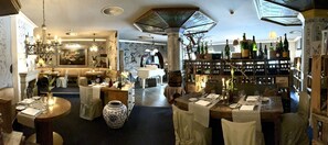 Restaurante com várias áreas de refeição, um bar com garrafas de vinho e um vaso grande nas mesas.