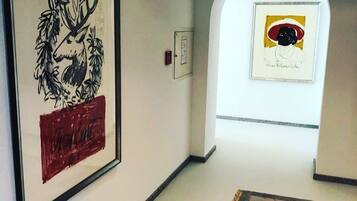 Um corredor com obras de arte emolduradas nas paredes, piso coberto por carpete e uma porta em arco que dá para outro cômodo.