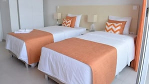 Quarto de hotel com duas camas, cada uma com roupa de cama branca e almofadas de laranja.