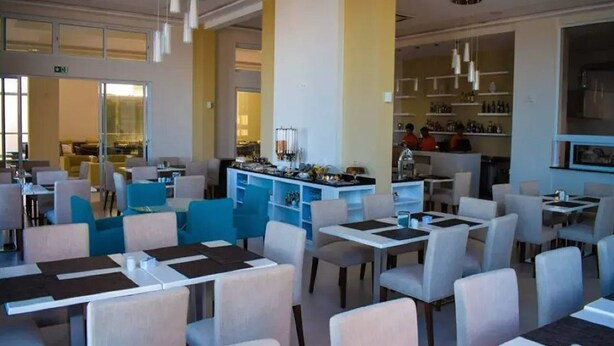 Um restaurante moderno com uma combinação de assentos em cabines e mesas, um bar e uma cozinha visível ao fundo.