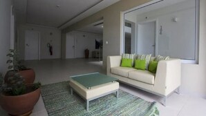 Uma sala de estar moderna com um sofá branco, almofadas verdes, uma mesa de centro de vidro e um espelho grande.