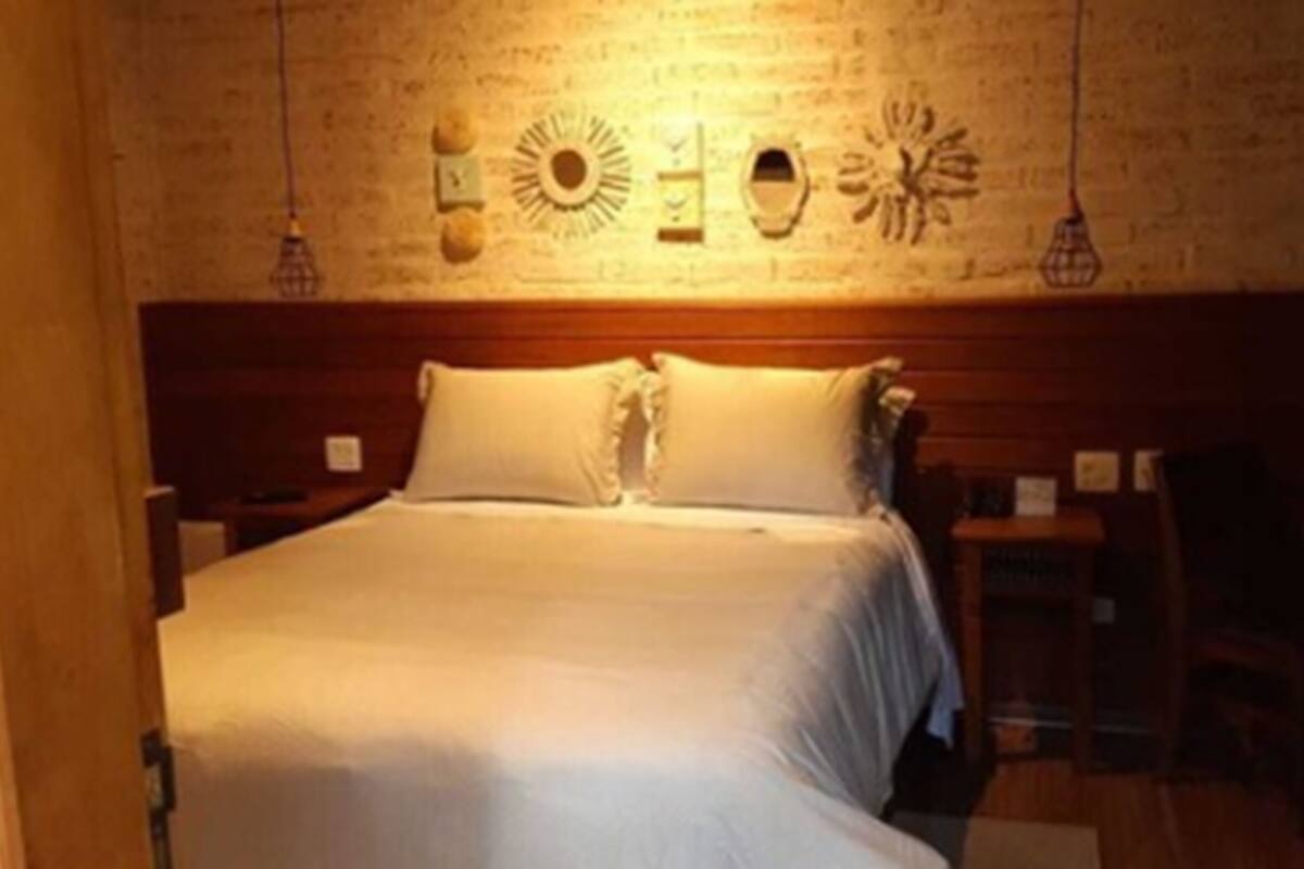 Cama bem arrumada em quarto com cabeceira de madeira e parede de tijolos.