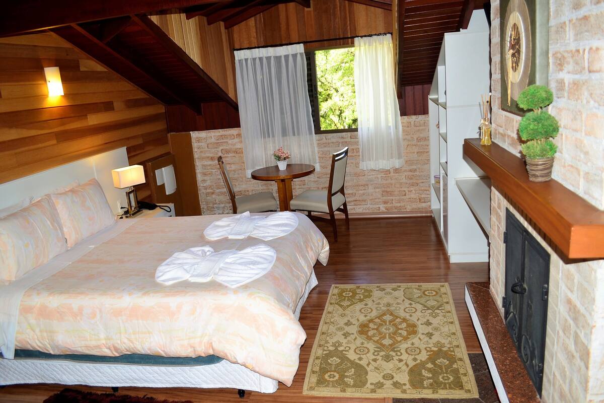 Um quarto aconchegante com uma cama grande, uma mesa redonda pequena e uma lareira.