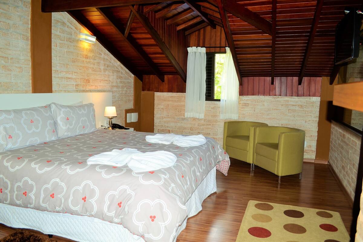 Quarto com uma cama grande, um sofá pequeno, teto de madeira e parede de tijolos.