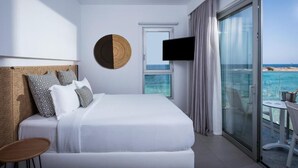 Quarto de hotel com cama, televisão, vista para o mar e varanda com mesa e cadeiras.
