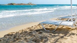 Uma praia com um guarda-sol de palha e espreguiçadeiras brancas.