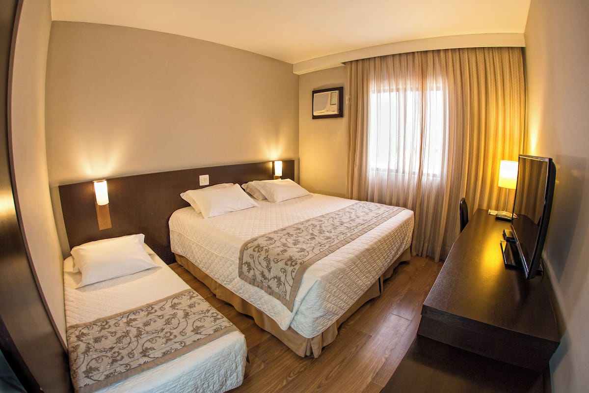 Quarto de hotel com duas camas, uma escrivaninha e uma luminária.