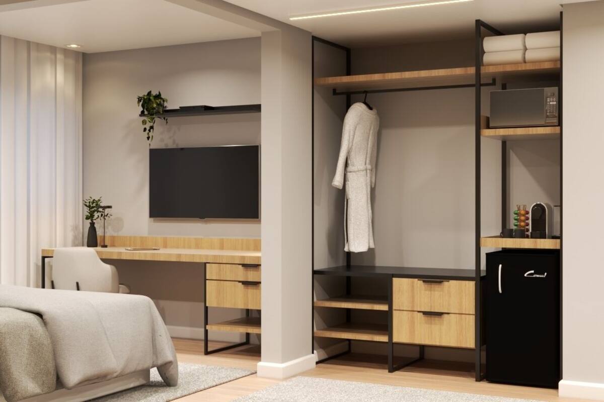 Quarto moderno com cama, escrivaninha, guarda-roupa, televisão e um frigorífico pequeno.