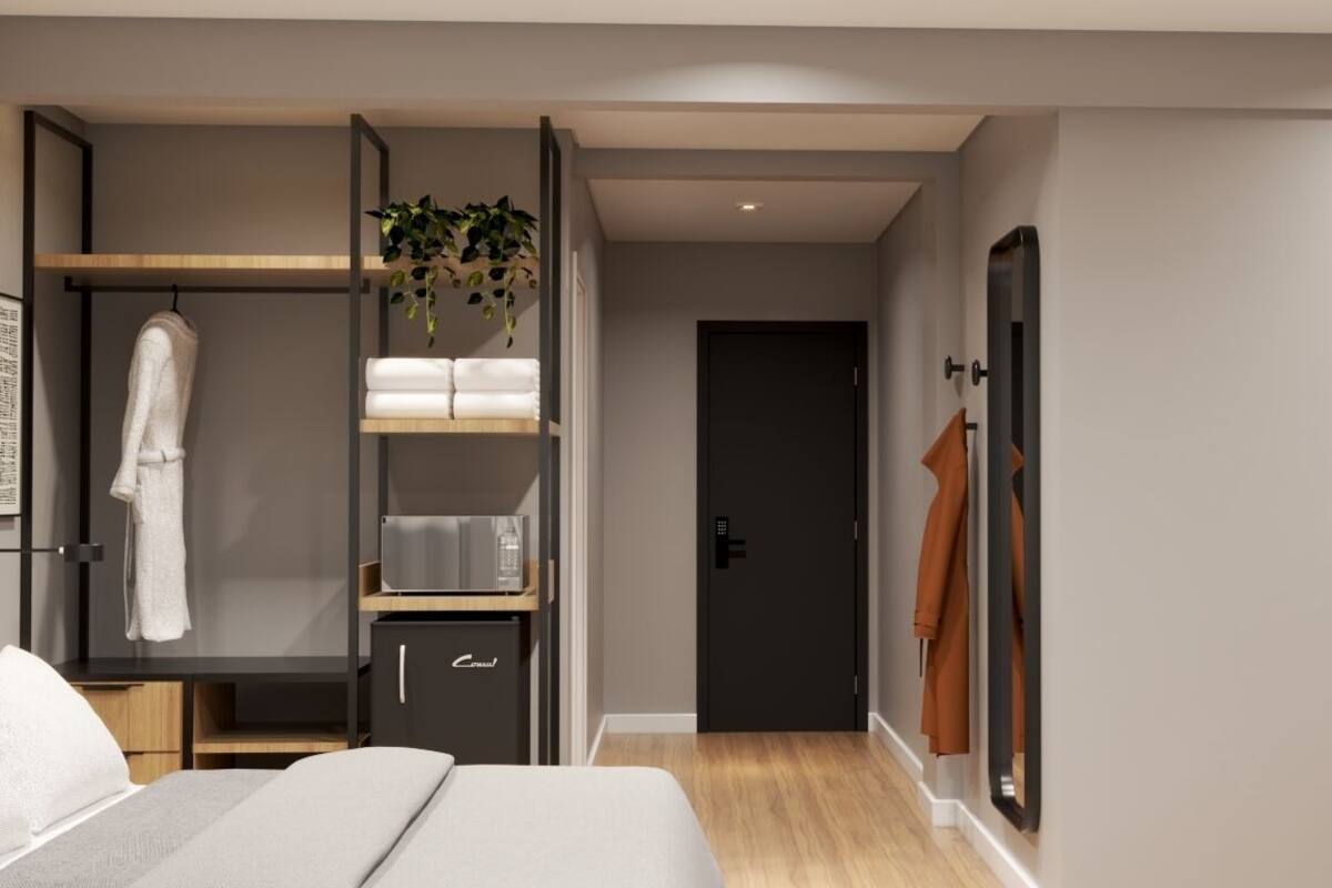 Quarto de hotel moderno com uma cama, um guarda-roupa, uma escrivaninha e uma porta que dá para outro espaço.