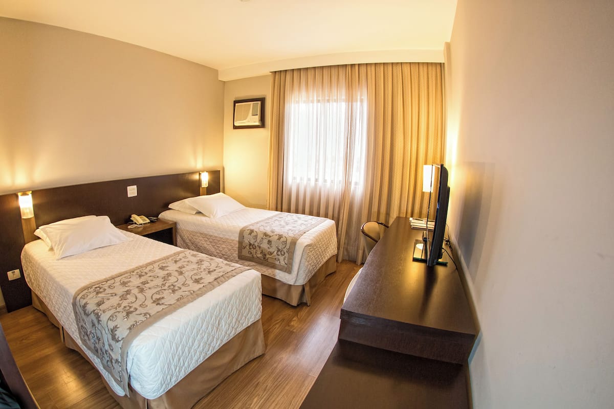 Quarto de hotel com duas camas, uma mesa, uma cadeira e uma televisão.