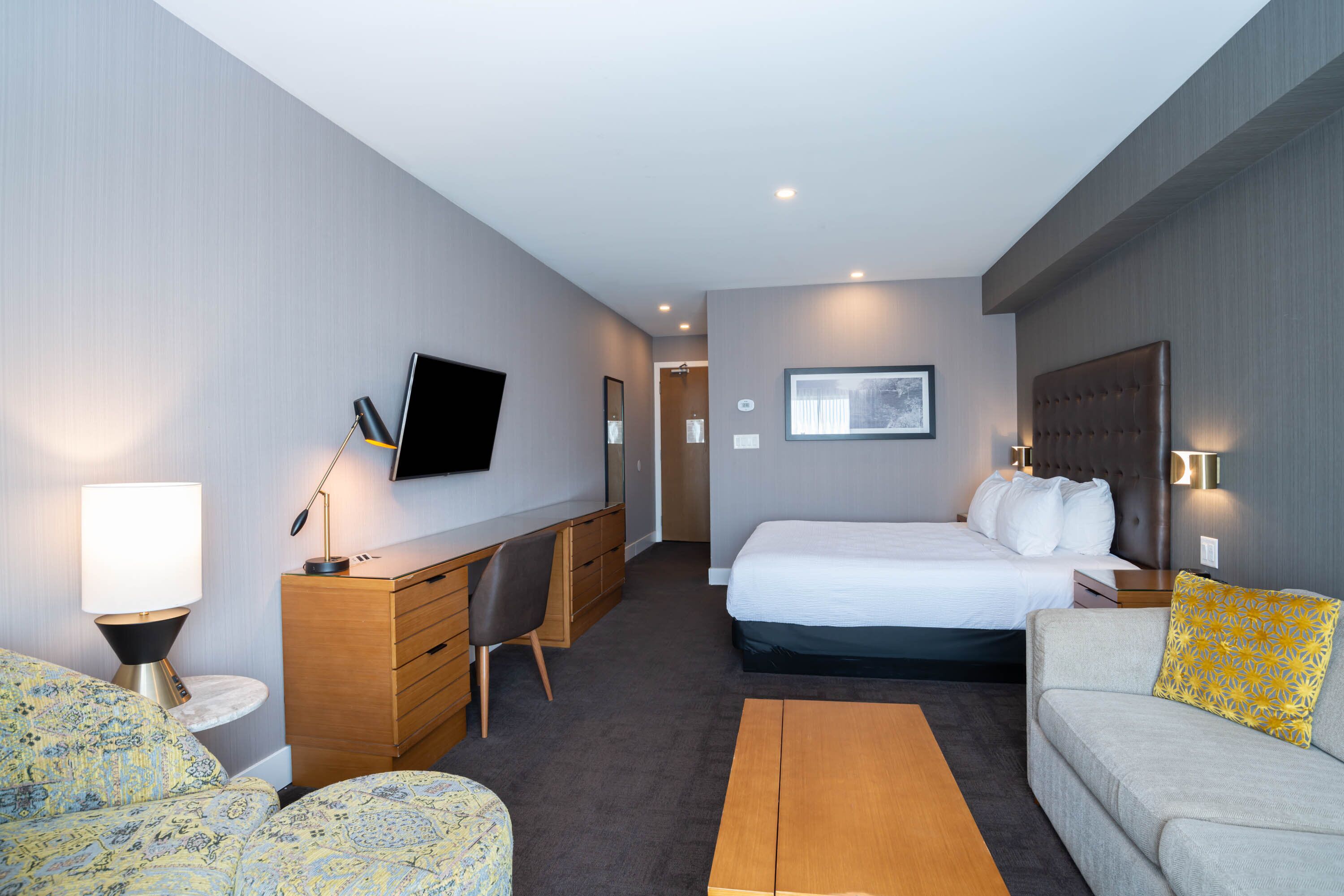 Quarto de hotel com cama, escrivaninha, cadeira, sofá e televisão.
