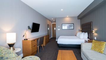 Quarto de hotel com cama, escrivaninha, cadeira, sofá e televisão.
