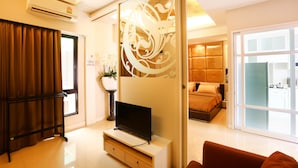 Quarto de hotel moderno com televisão de tela plana sobre um console de madeira, porta de vidro deslizante para uma varanda e um painel decorativo grande na parede.
