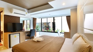 Quarto de hotel com uma cama grande, uma escrivaninha com televisão, um frigorífico pequeno e uma janela com cortinas.