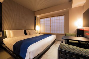 Quarto de hotel com cama, escrivaninha, cadeira e uma janela grande com vista.
