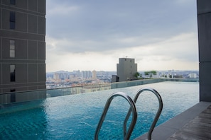 Piscina infinita no terraço com vista para a cidade, escada de metal e guarda-corpo de vidro.