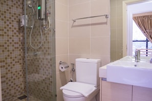 Casa de banho com cabine de chuveiro em vidro, sanita e lavatório com espelho.