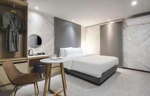 Quarto de hotel moderno com cama, mesa de cabeceira, cadeira e toucador com espelho e roupão.