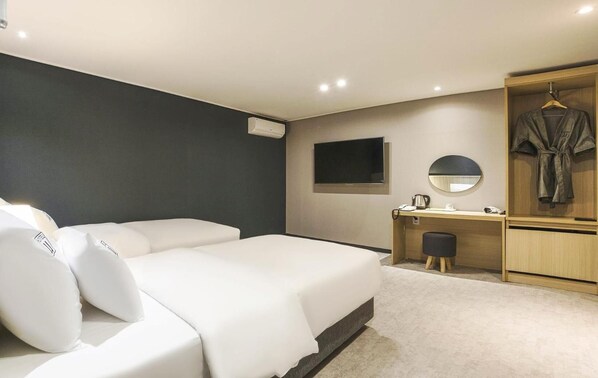 Quarto de hotel moderno com uma cama grande, uma escrivaninha, um espelho e um roupão pendurado num guarda-roupa de madeira.