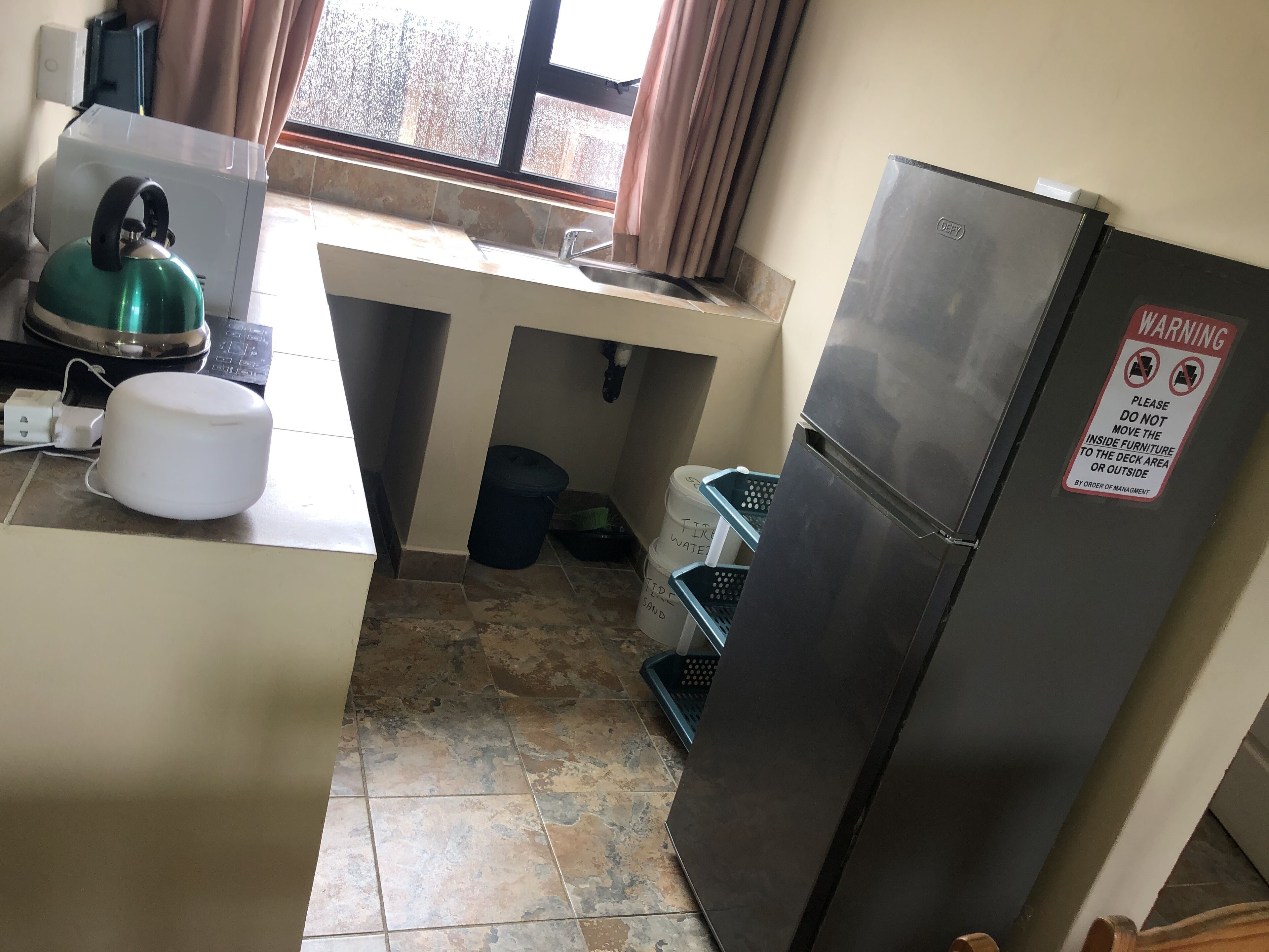 Uma cozinha compacta com geladeira, chaleira e pia.