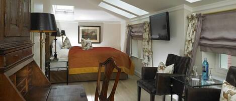 Quarto com cama, escrivaninha, cadeira, televisão e claraboia.