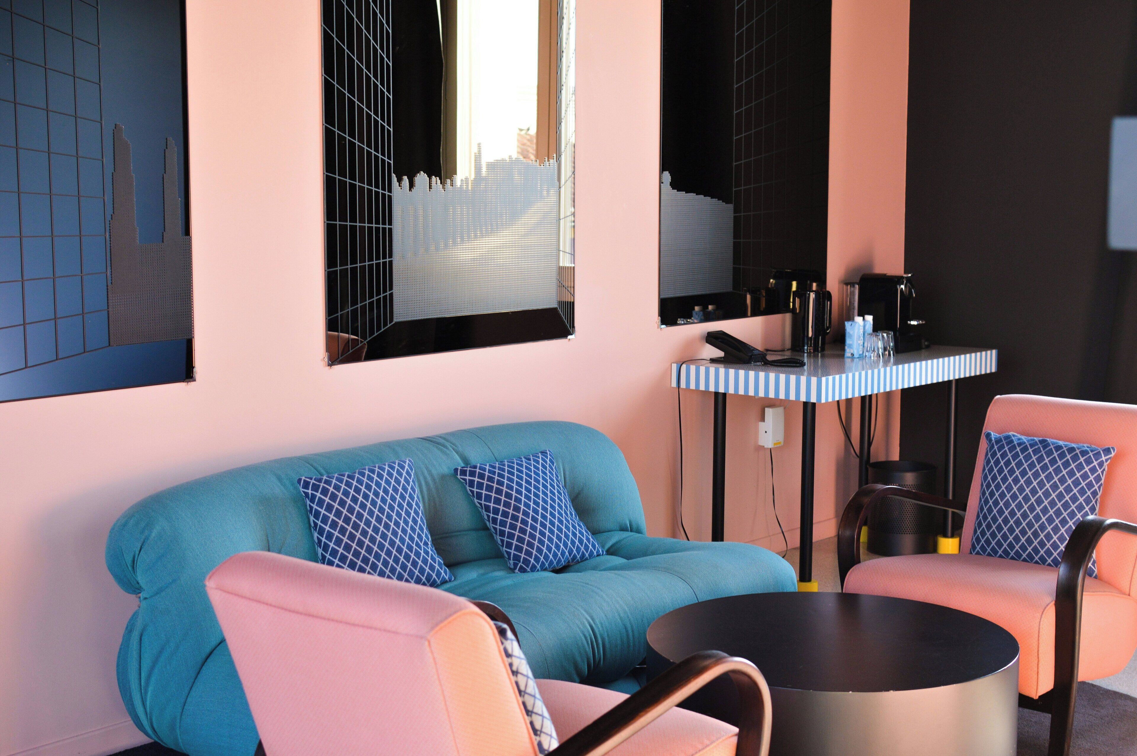 Quarto moderno com sofá verde-água, poltrona rosa, mesa de centro redonda e pequena mesa lateral com cafeteira.