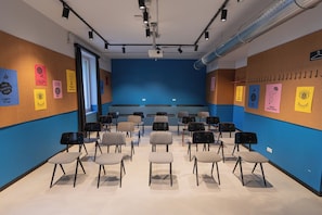 Uma sala de conferências com fileiras de cadeiras, uma tela de projetor e cartazes motivacionais nas paredes.