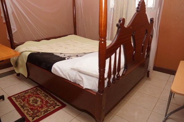 Uma cama de madeira com dossel, uma mesa de cabeceira e um tapete vermelho estampado.