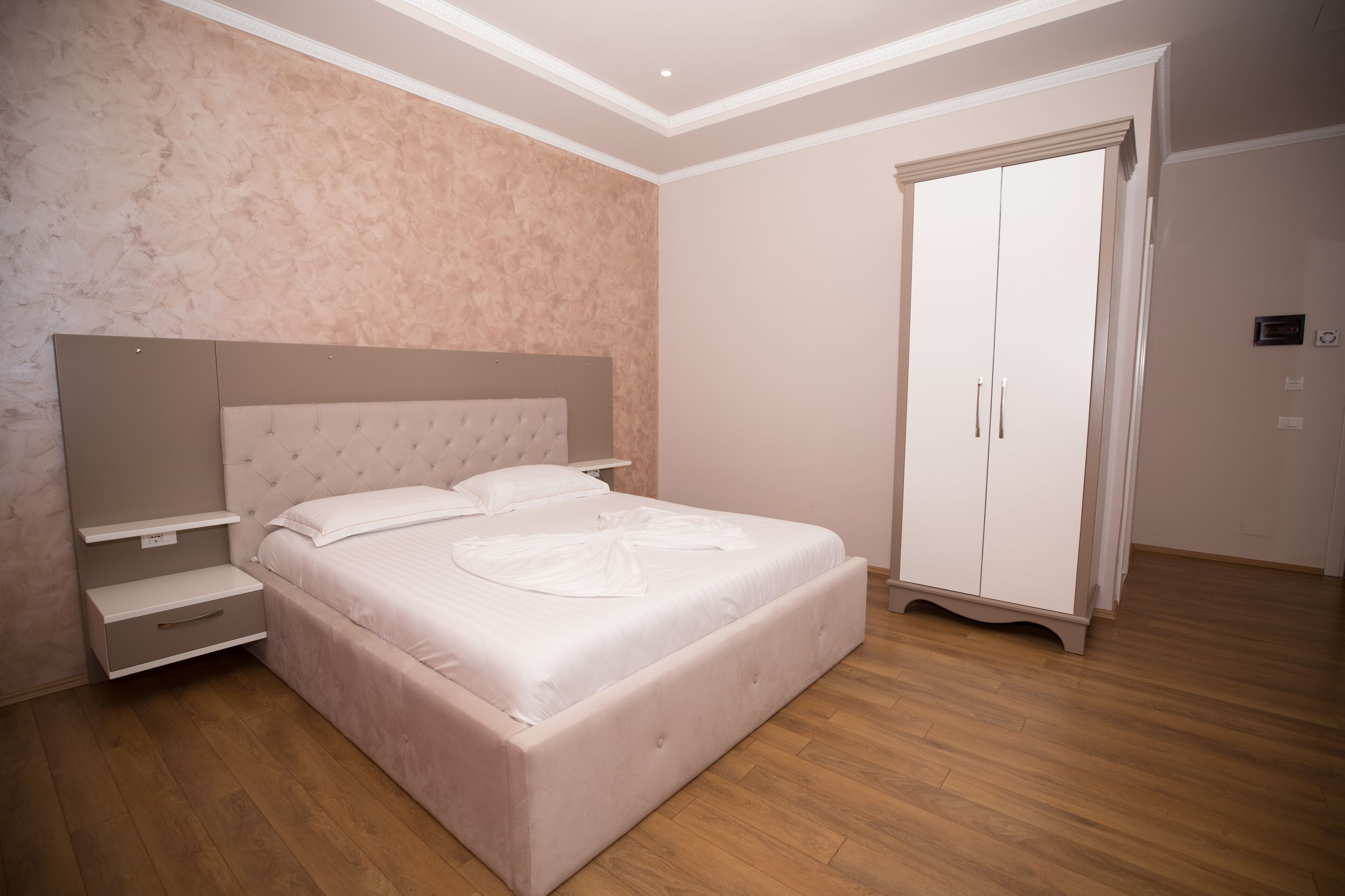 Quarto com cama grande, mesa de cabeceira, guarda-roupa e prateleira embutida.