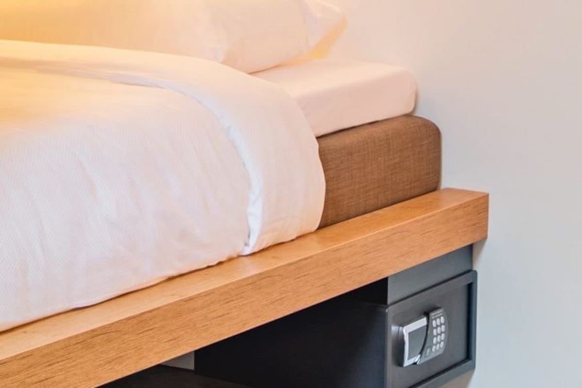 Uma cama com cabeceira de madeira e cofre embutido.