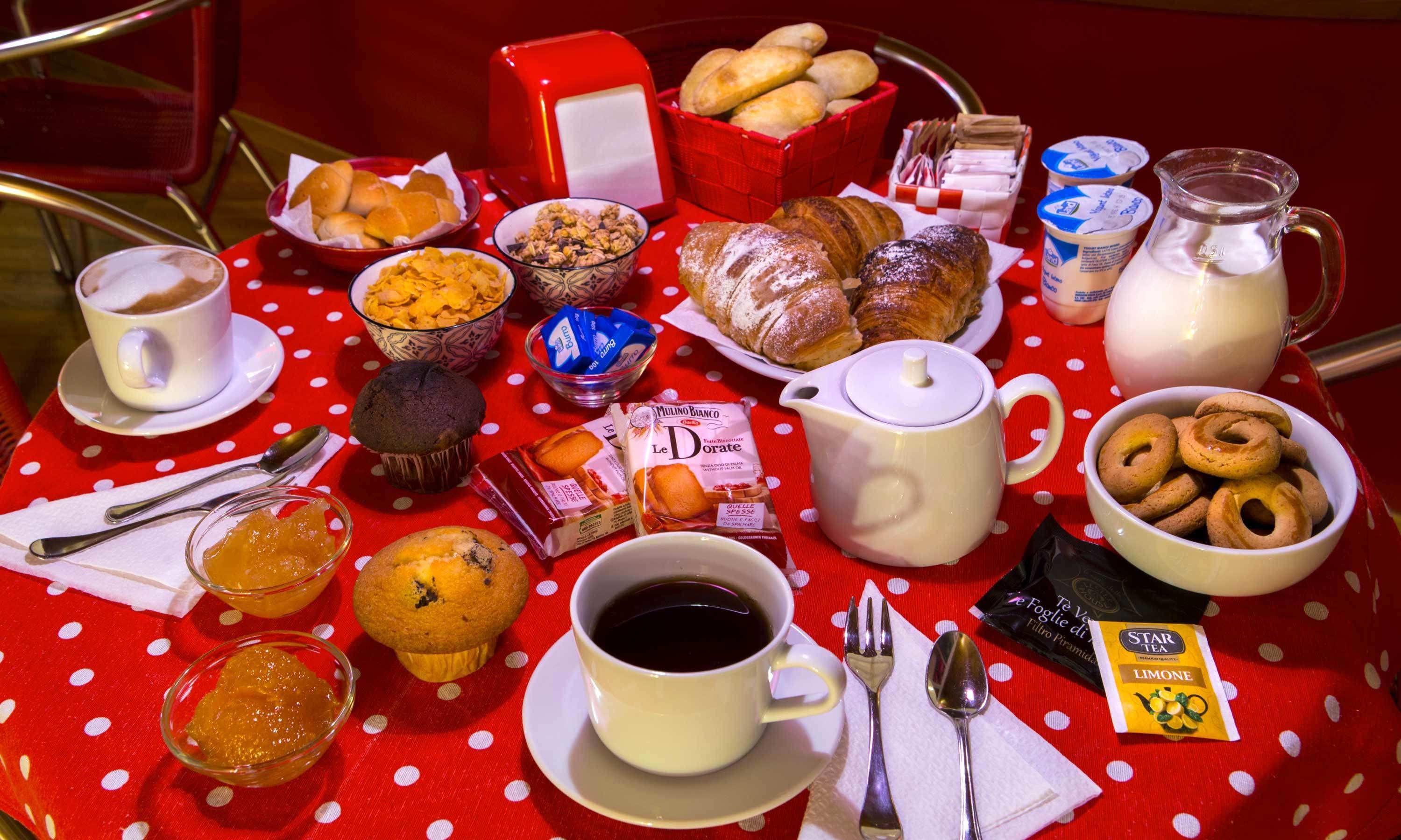 Uma mesa de café da manhã com diversos alimentos, uma xícara de café, um bule de chá e um jarro de leite.