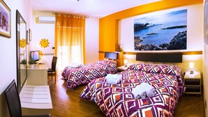 Quarto de hotel com duas camas, uma escrivaninha, uma cadeira, televisão e uma janela grande com vista para o litoral.