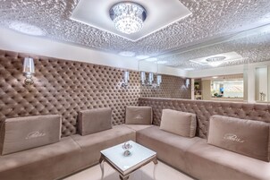 Uma sala de estar luxuosa com um sofá bege com capitonê, uma pequena mesa de centro quadrada e um candelabro.