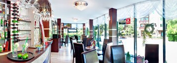 Restaurante com área de bar, mesas e grandes janelas com vista para a rua.