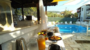 Uma mesa posta para o café da manhã, com cafeteira, jarra de suco e uma tigela de frutas.