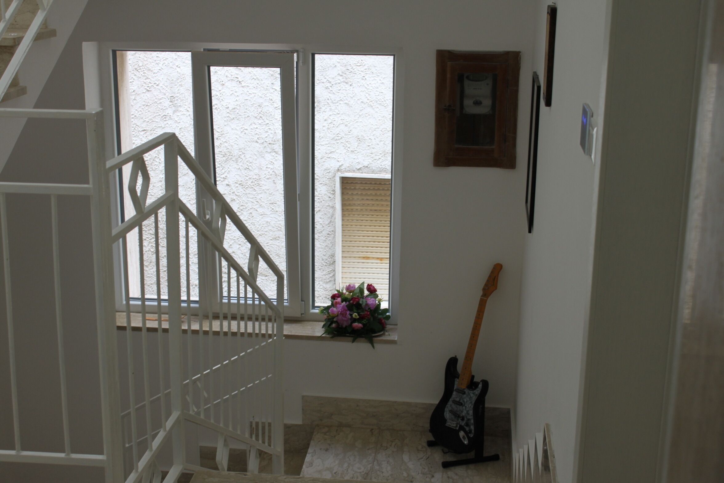 Uma escada leva a um patamar com uma janela, um violão e um quadro na parede.