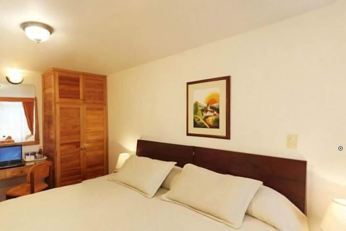 Quarto com cama, escrivaninha, cadeira, guarda-roupa e um quadro na parede.