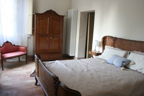 Quarto com cama de madeira, uma cadeira vermelha, um guarda-roupa e um radiador.