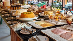 Buffet com diversos pratos em ambiente tropical, com vigas de madeira e plantas.
